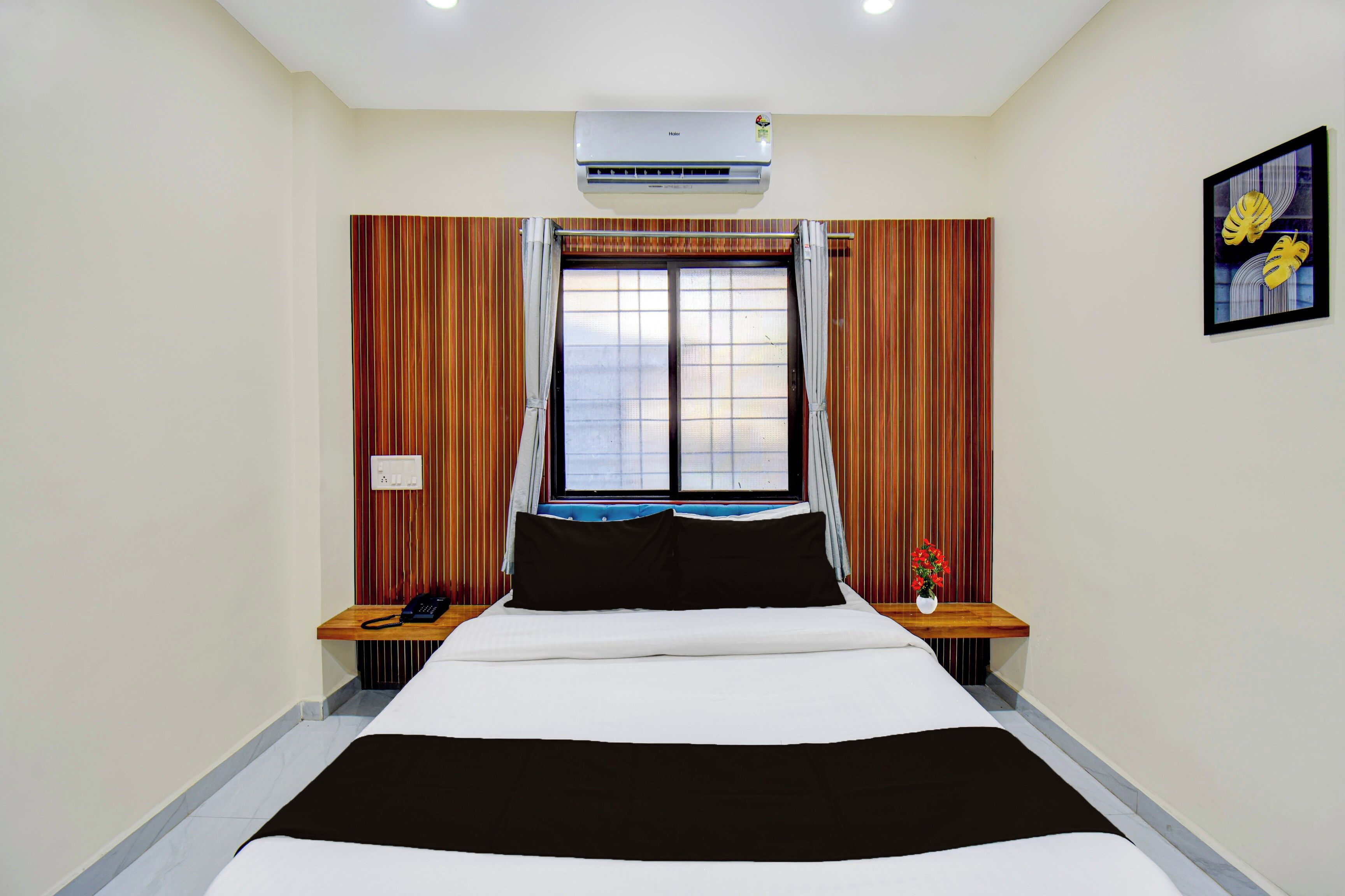 Quarto de hotel com cama, mesa de cabeceira com telefone, janela com cortinas, aparelho de ar condicionado e quadro na parede.