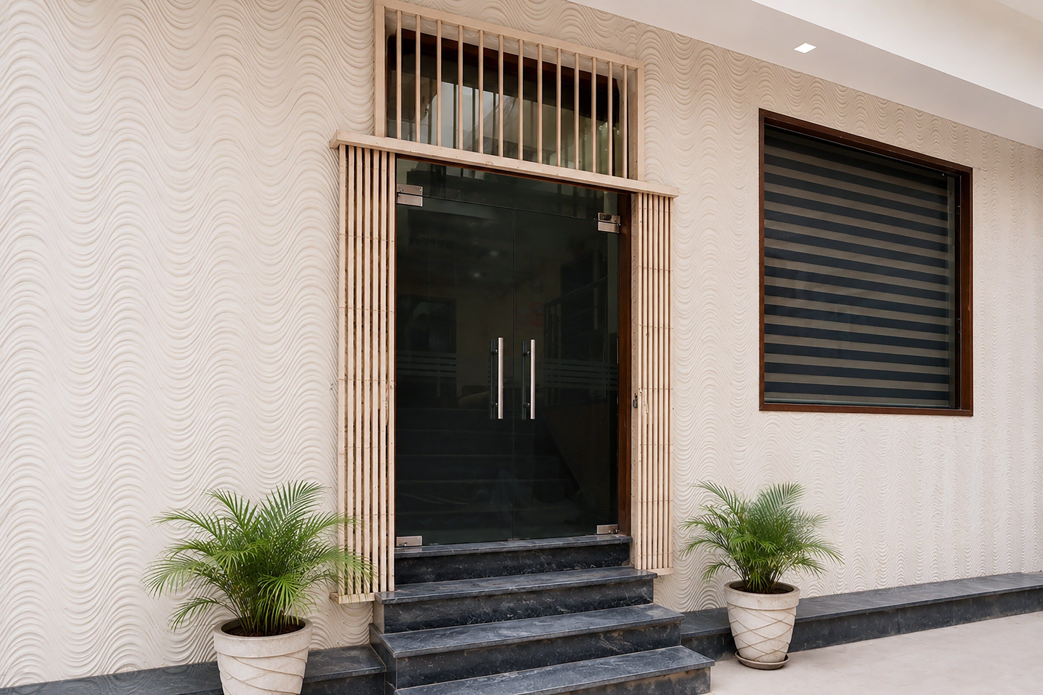 Entrada de um edifício com porta de vidro, escadas e dois vasos de plantas.