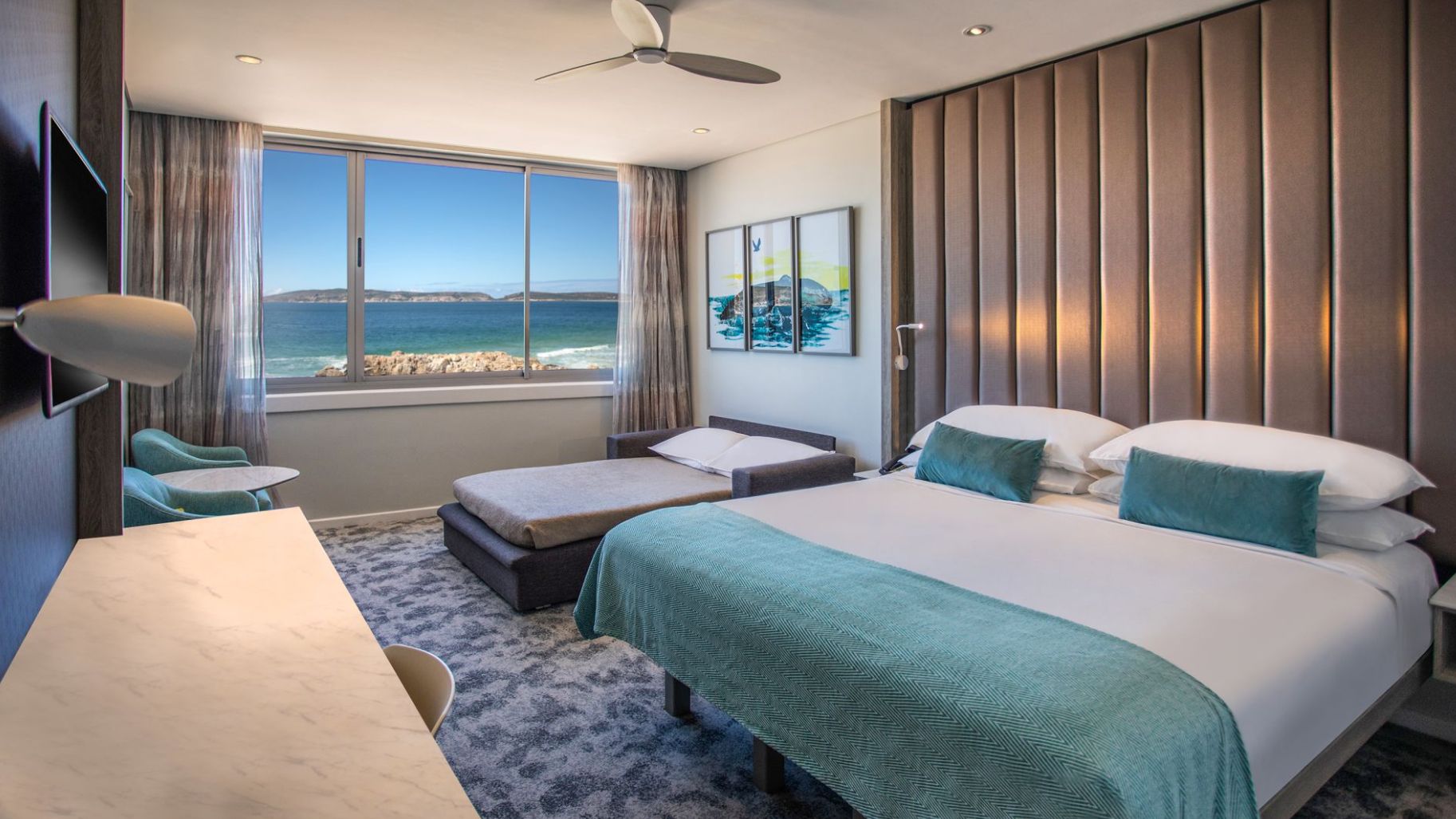 Quarto de hotel com uma cama grande, uma escrivaninha e vista para o mar.