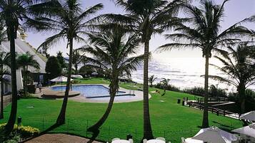Área de piscina com palmeiras, mobiliário ao ar livre e vista para o oceano.