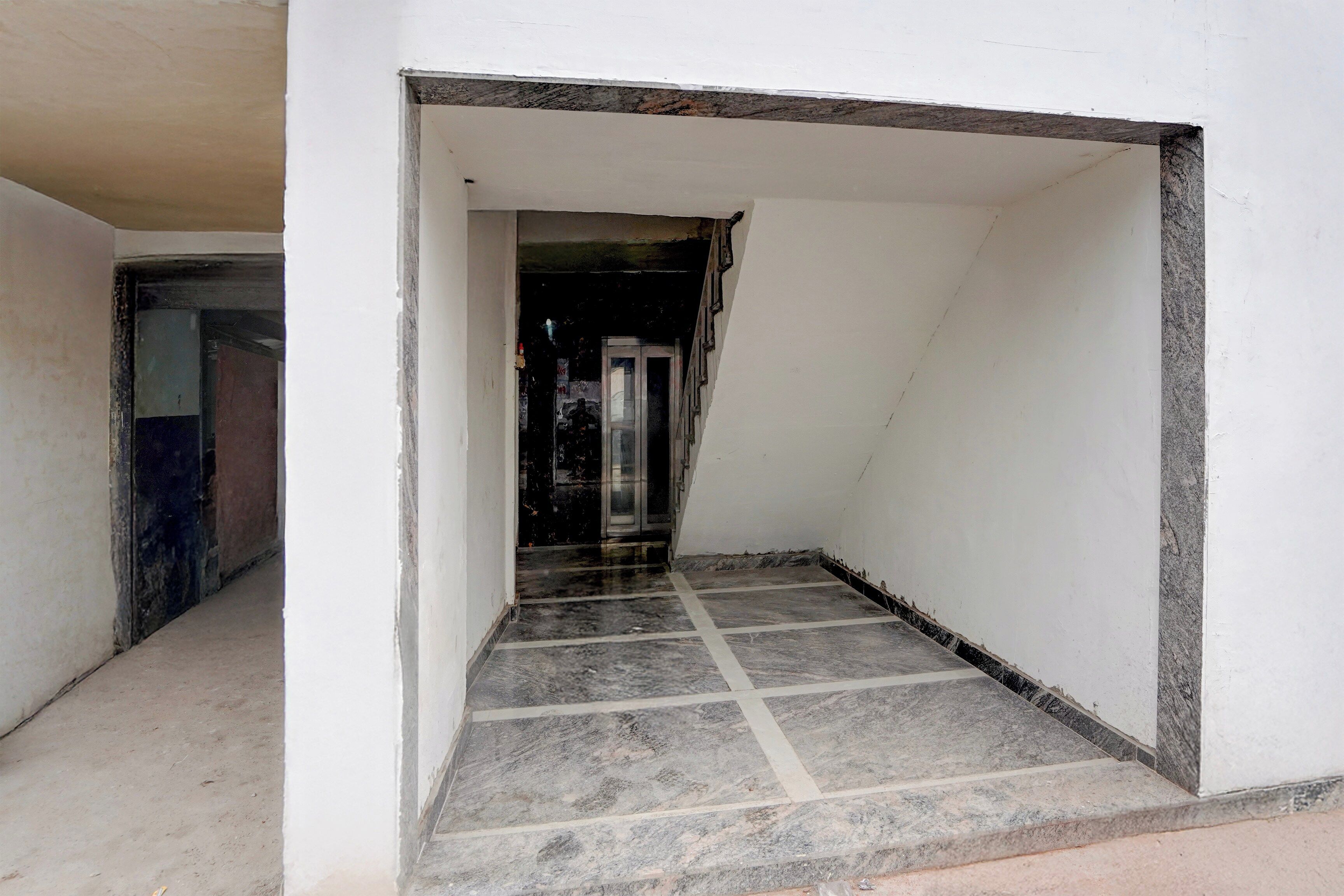 Um corredor estreito com piso de azulejos que leva a um espaço interno escuro.