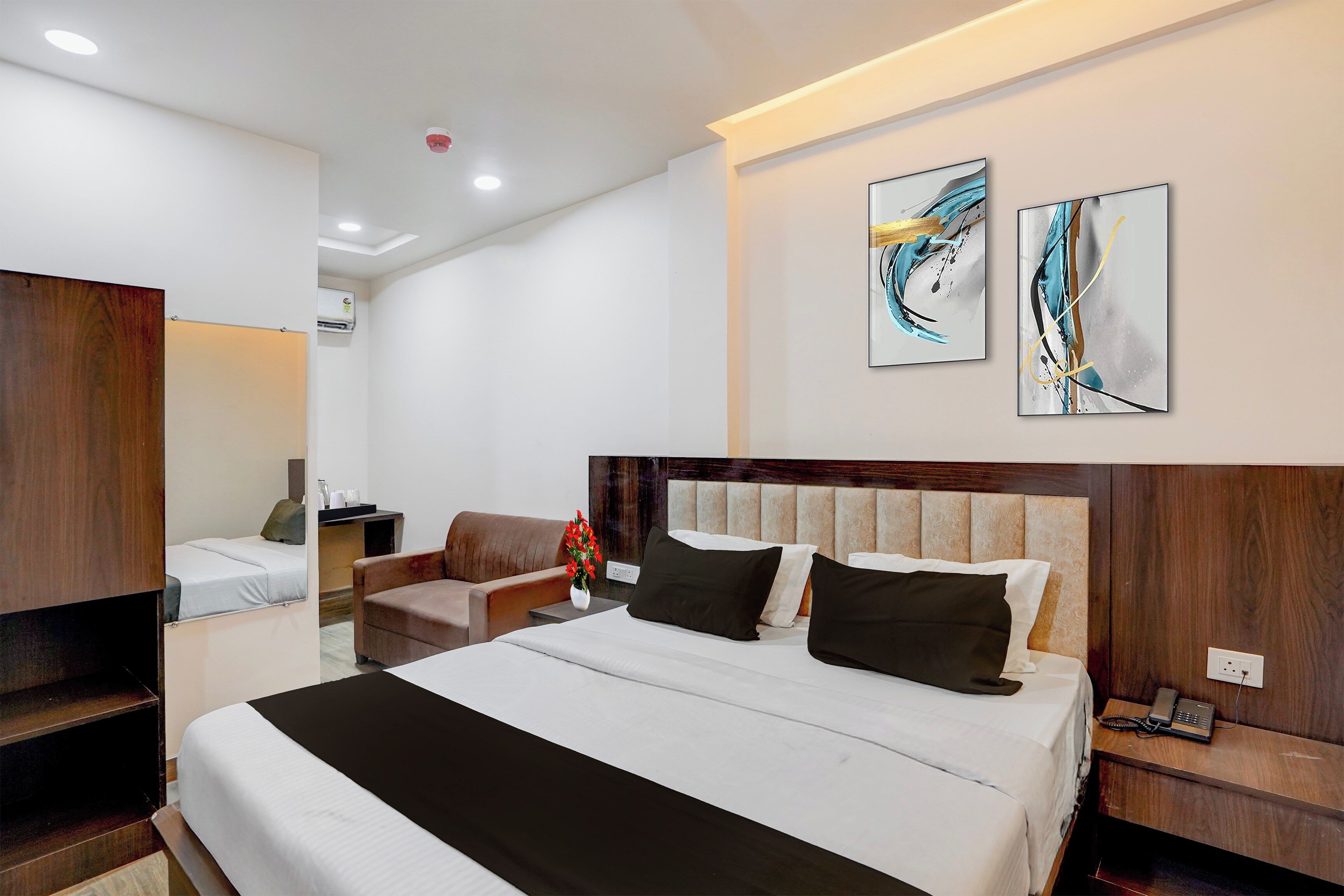 Quarto de hotel com uma cama grande, cabeceira de madeira, escrivaninha com telefone e duas pinturas abstratas na parede.