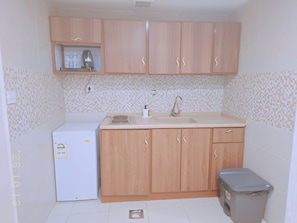 Cozinha compacta com armários de madeira, geladeira branca, pia e lixeira.