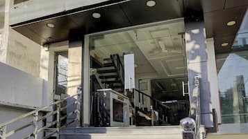 Entrada de um edifício moderno com porta de vidro, escadas e corrimão de metal.