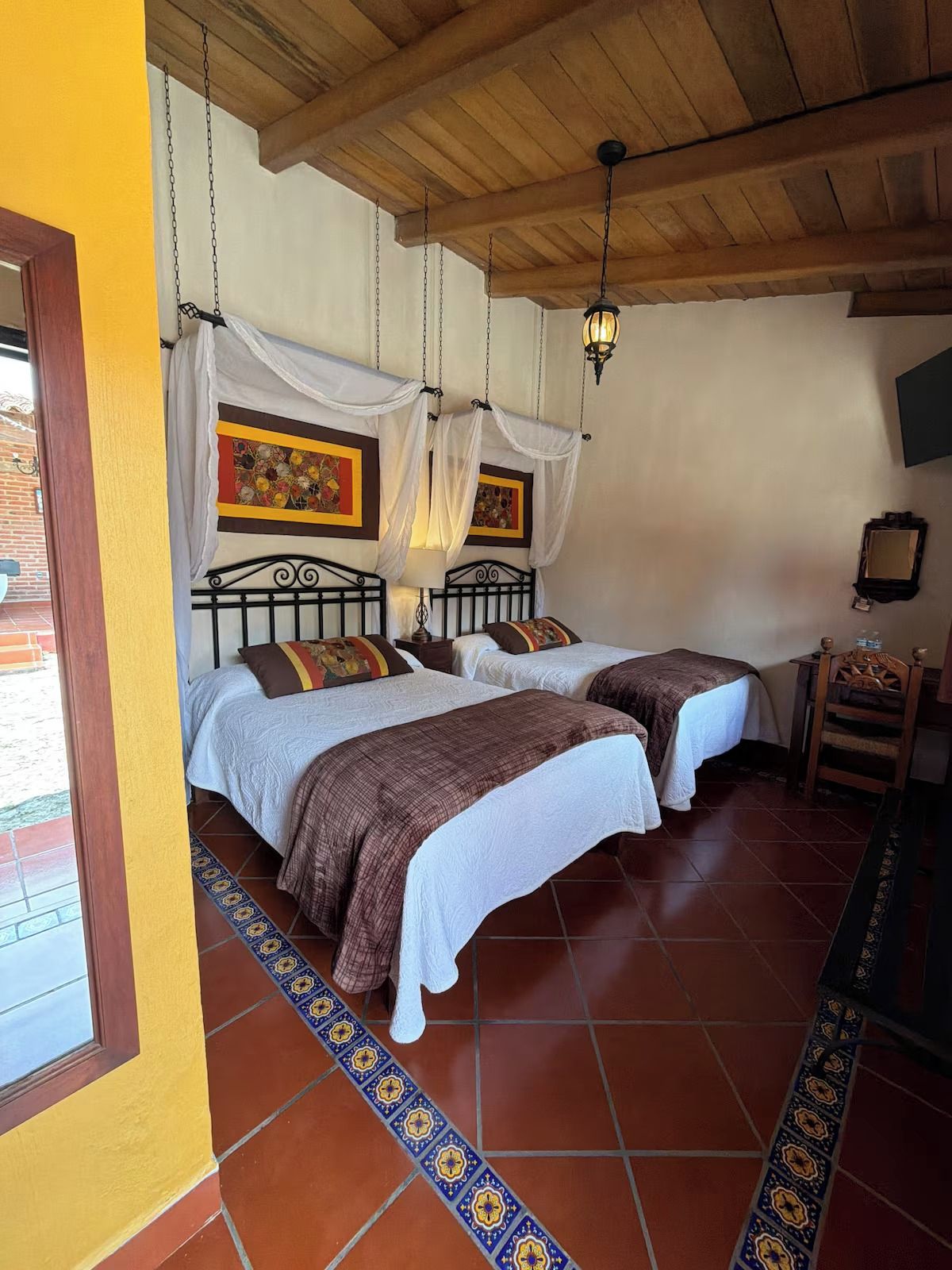 Quarto com duas camas, teto de madeira e piso estampado.