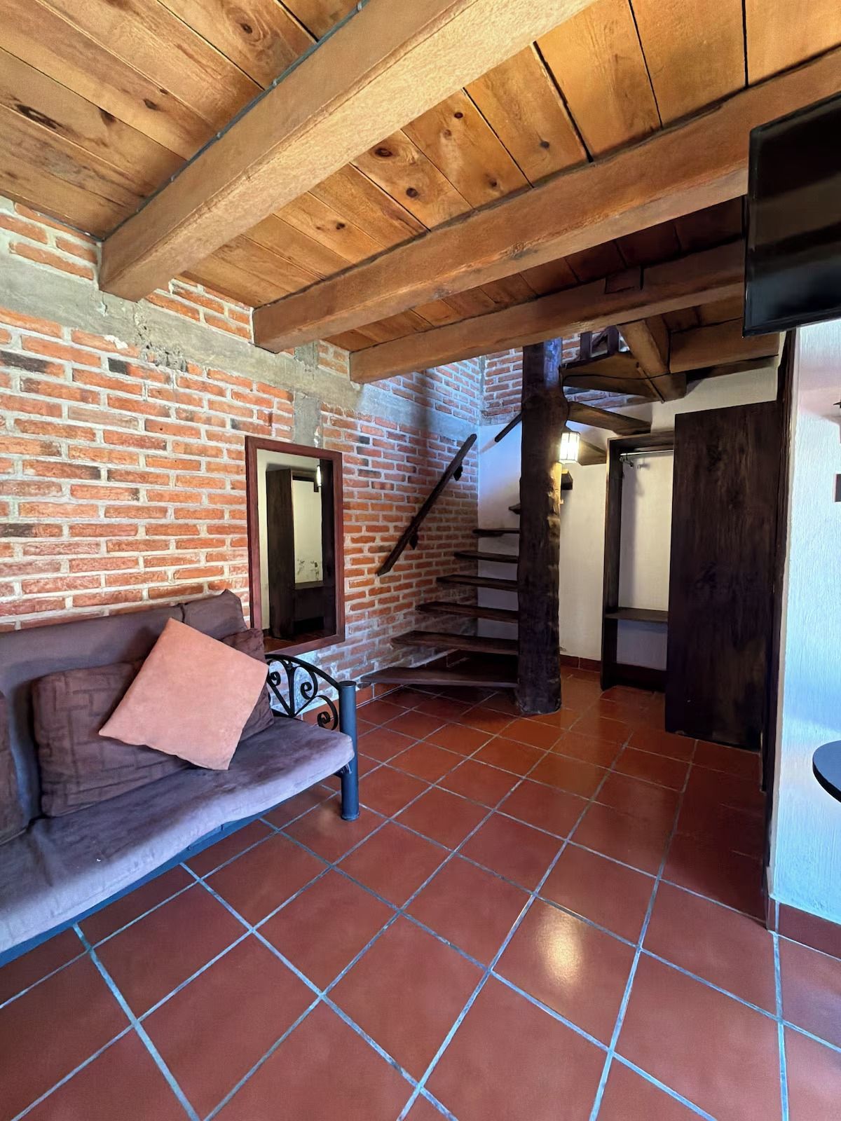 Um interior rústico com parede de tijolos, vigas de madeira, escada e piso de azulejos.