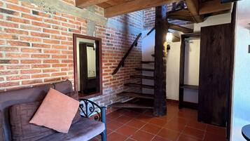 Um interior rústico com parede de tijolos, vigas de madeira, escada e piso de azulejos.