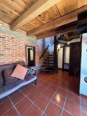 Um interior rústico com parede de tijolos, vigas de madeira, escada e piso de azulejos.