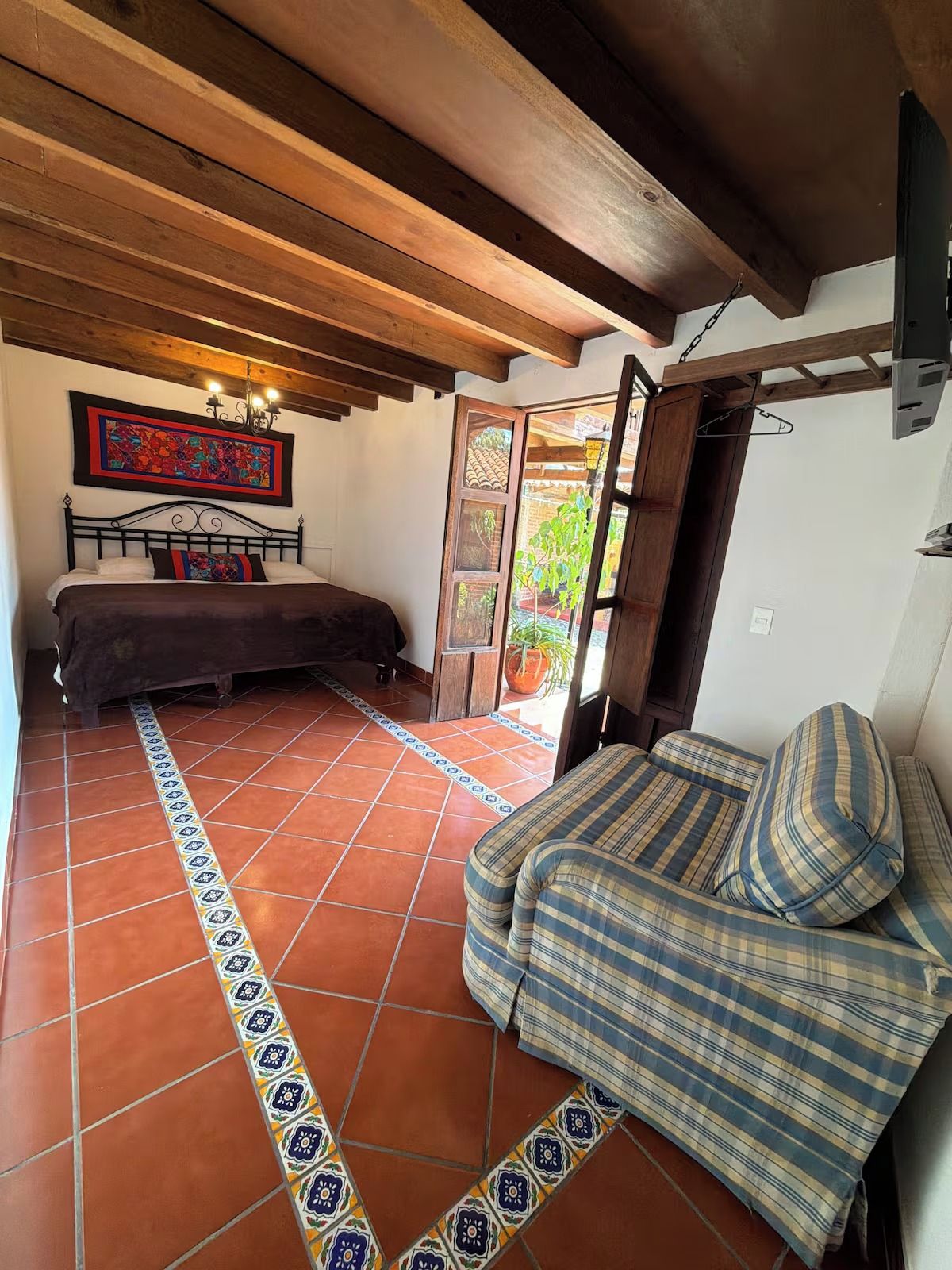 Quarto com cama, sofá, piso de azulejos, teto de madeira e porta que dá para o exterior.