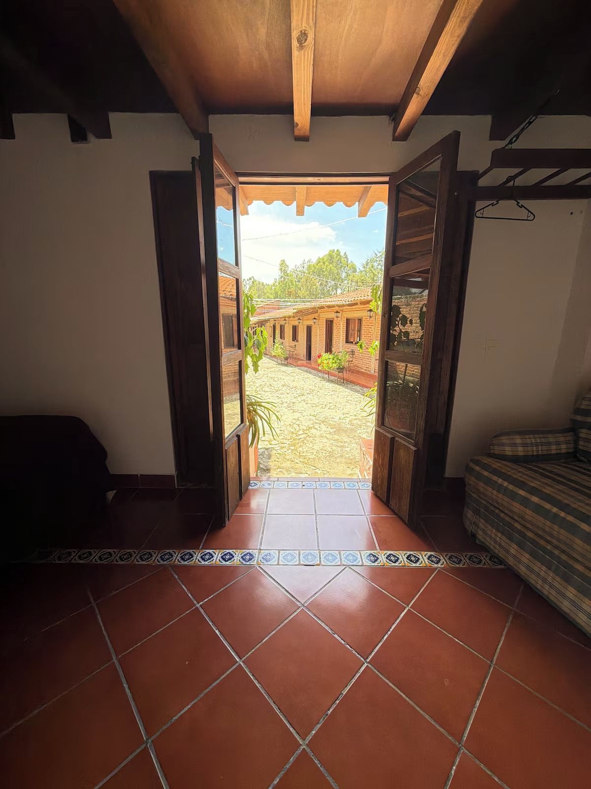 Abertura de porta que dá para um pátio com chão de azulejos e cama com colcha listrada.