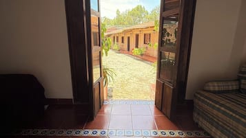 Abertura de porta que dá para um pátio com chão de azulejos e cama com colcha listrada.