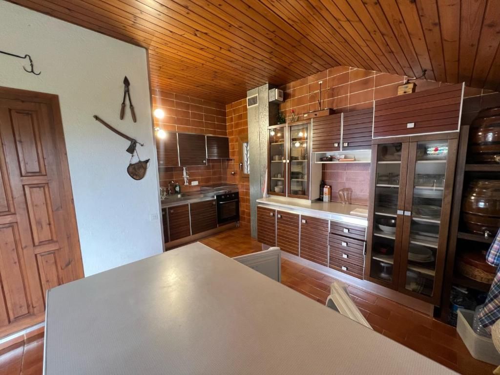 Cozinha com teto e armários de madeira, bancada branca e um suporte para panelas pendurado.