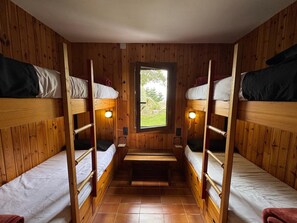 Quarto com três beliches, uma mesinha e janela com vista para o exterior.