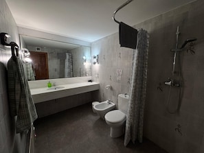 Uma casa de banho moderna com um espelho grande, sanita, bidé e chuveiro.