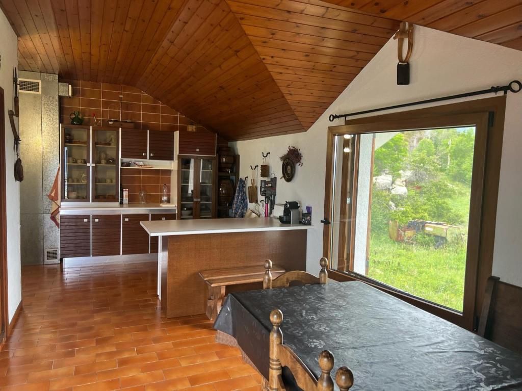 Cozinha espaçosa com armários de madeira e uma ilha grande, área de jantar com mesa de madeira, e uma janela ampla com vista para vegetação.