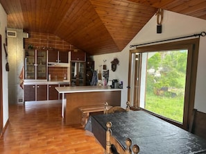 Cozinha espaçosa com armários de madeira e uma ilha grande, área de jantar com mesa de madeira, e uma janela ampla com vista para vegetação.