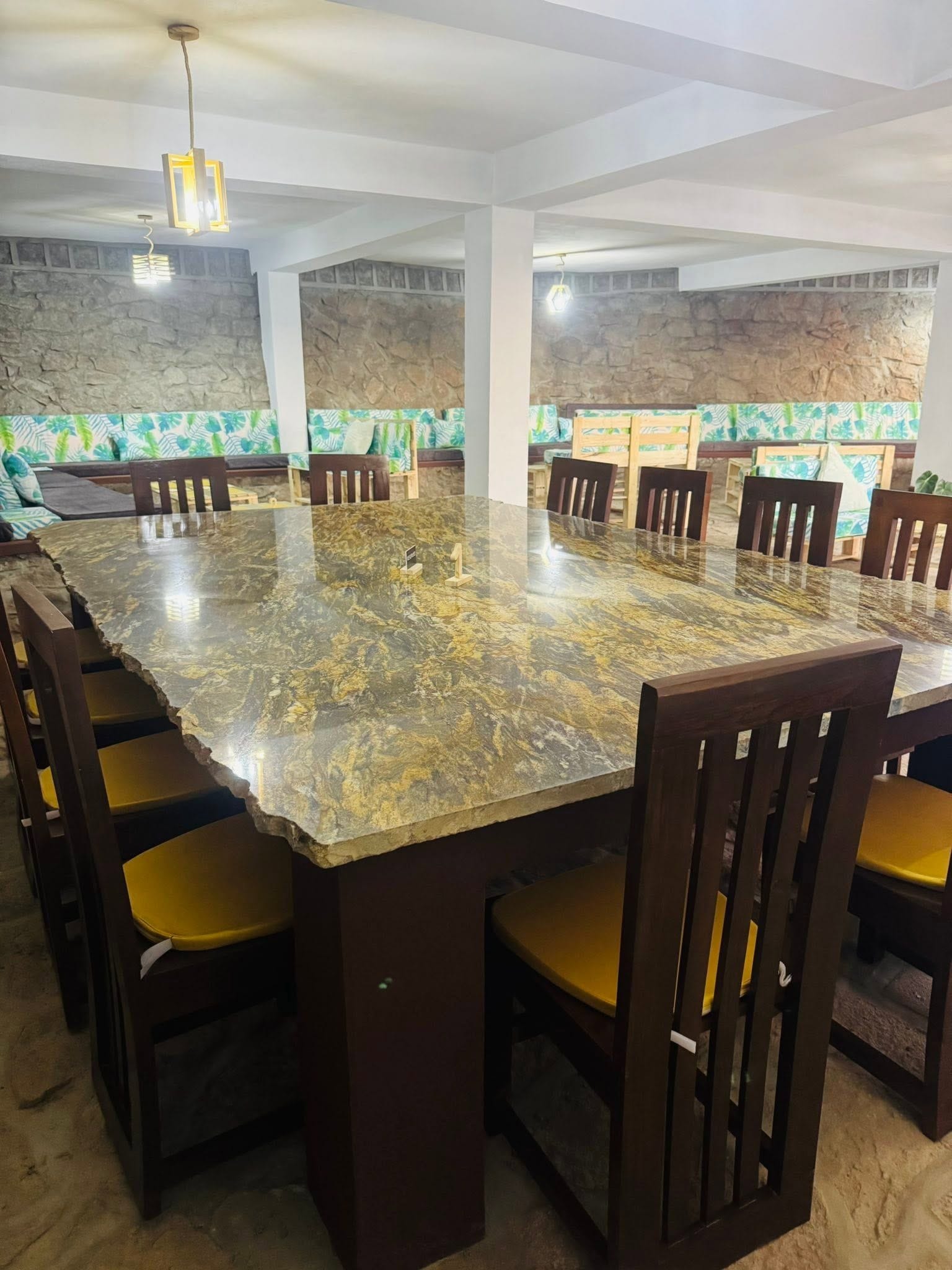 Uma grande mesa oval de conferência com cadeiras, uma parede de pedra e um lustre.