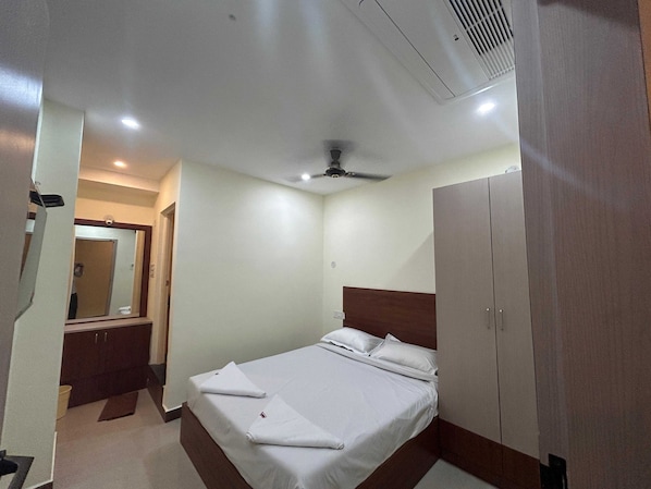 Quarto de hotel com cama, guarda-roupa, espelho e ventoinha no teto.