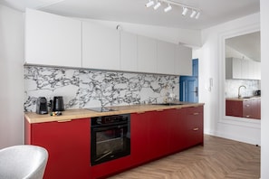 Cozinha moderna com painel de parede em mármore, armários vermelhos e forno embutido.