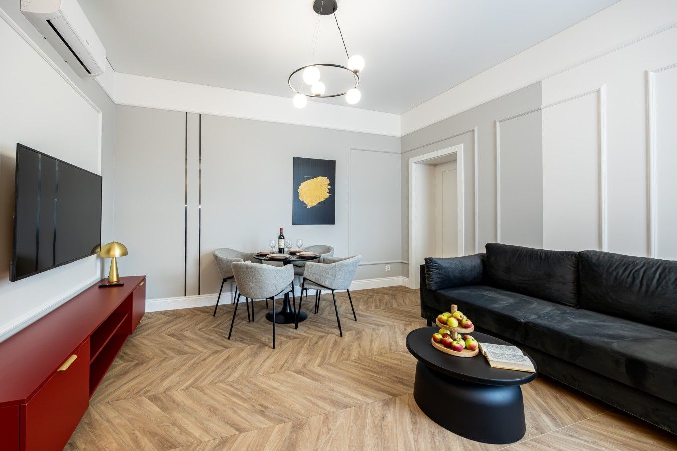 Uma sala de estar moderna com televisão de tela plana, uma mesa de jantar com cadeiras, um sofá de couro preto e uma mesa de centro com maçãs e um livro.