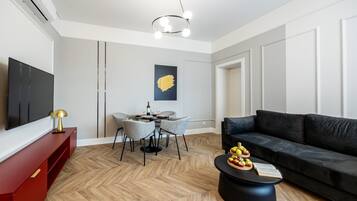Uma sala de estar moderna com televisão de tela plana, uma mesa de jantar com cadeiras, um sofá de couro preto e uma mesa de centro com maçãs e um livro.