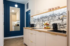 Uma cozinha moderna com revestimento de mármore, um expositor de frutas em dois níveis e uma cafeteira.