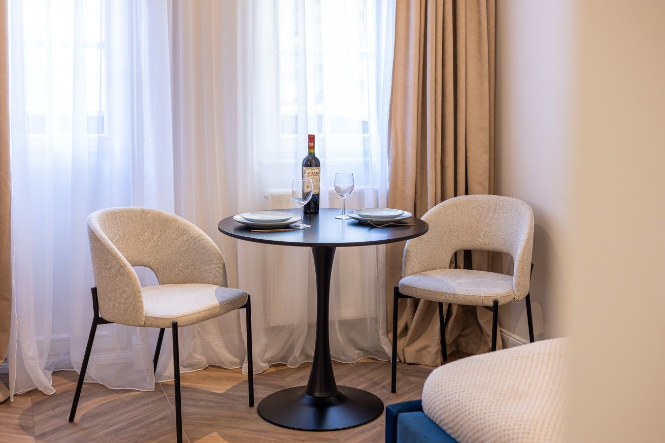 Quarto com uma mesa redonda posta para dois, duas cadeiras, uma garrafa de vinho e um copo sobre a mesa.