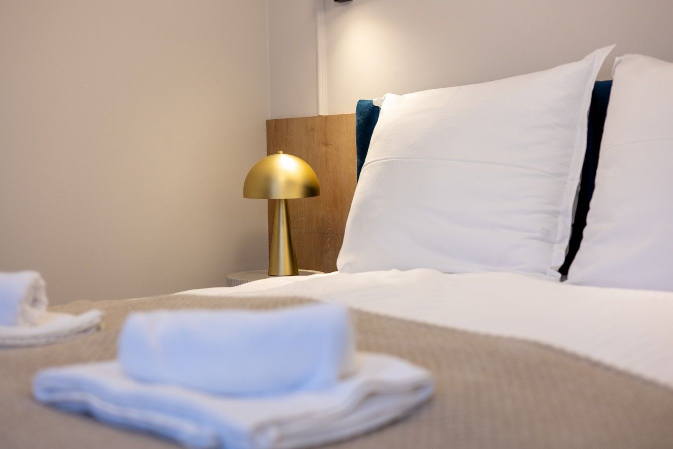 Quarto de hotel com cama bem arrumada, abajur e toalha dobrada sobre a cama.