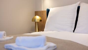 Quarto de hotel com cama bem arrumada, abajur e toalha dobrada sobre a cama.