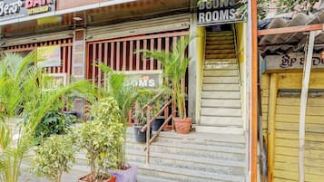 Um edifício com bar e quartos no andar térreo, rodeado por plantas em vasos.