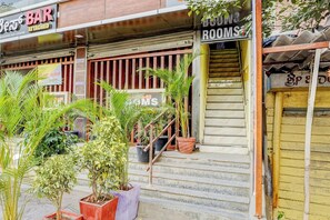 Um edifício com bar e quartos no andar térreo, rodeado por plantas em vasos.