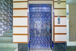 Um elevador com portão de metal, visor digital e parede revestida com padrão geométrico.