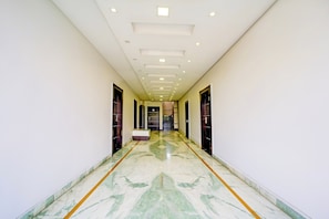 Um corredor comprido e estreito com chão de mármore e várias portas de ambos os lados.