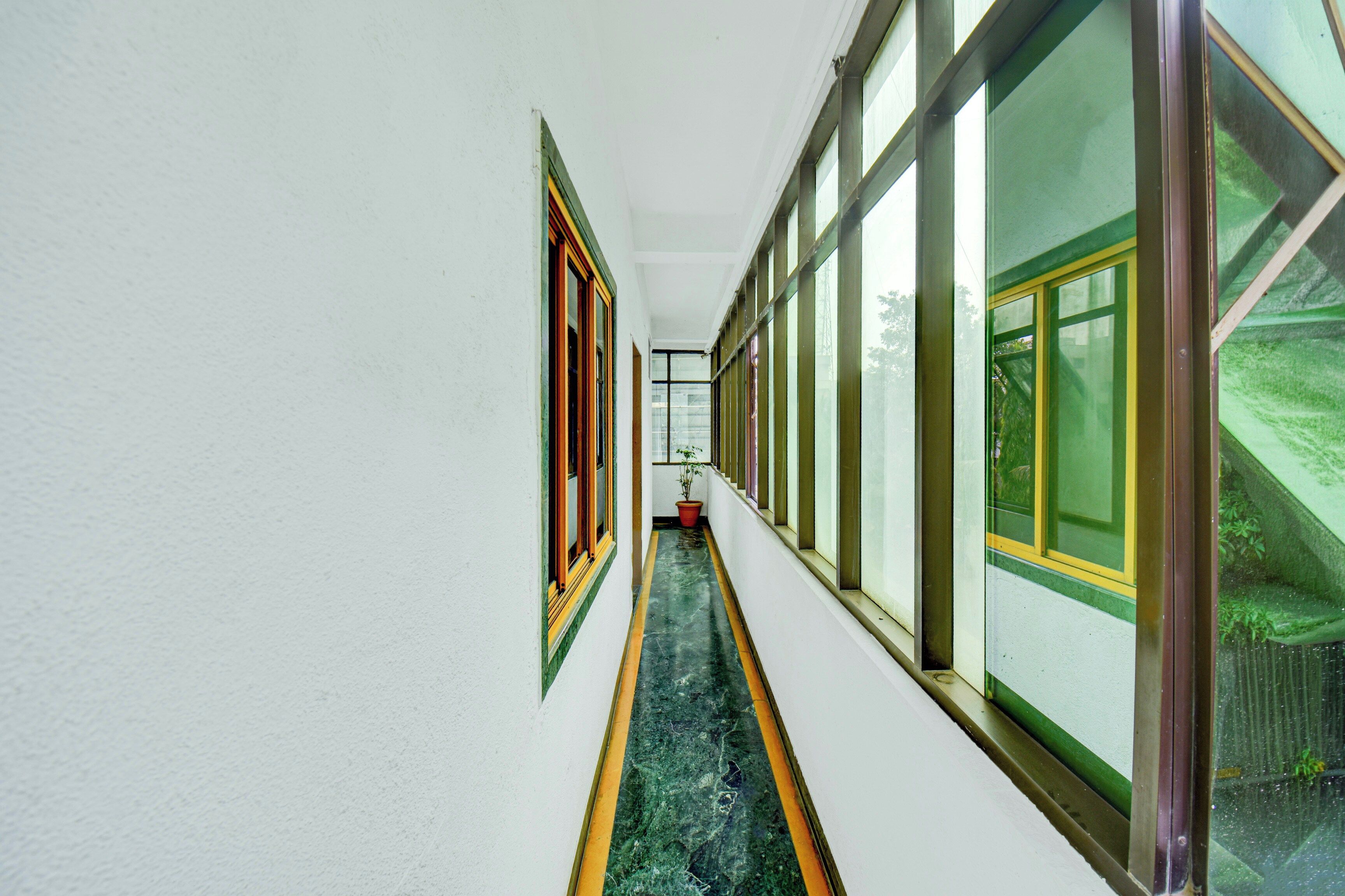 Um corredor com grandes janelas em ambos os lados, um vaso de planta e uma placa na parede.