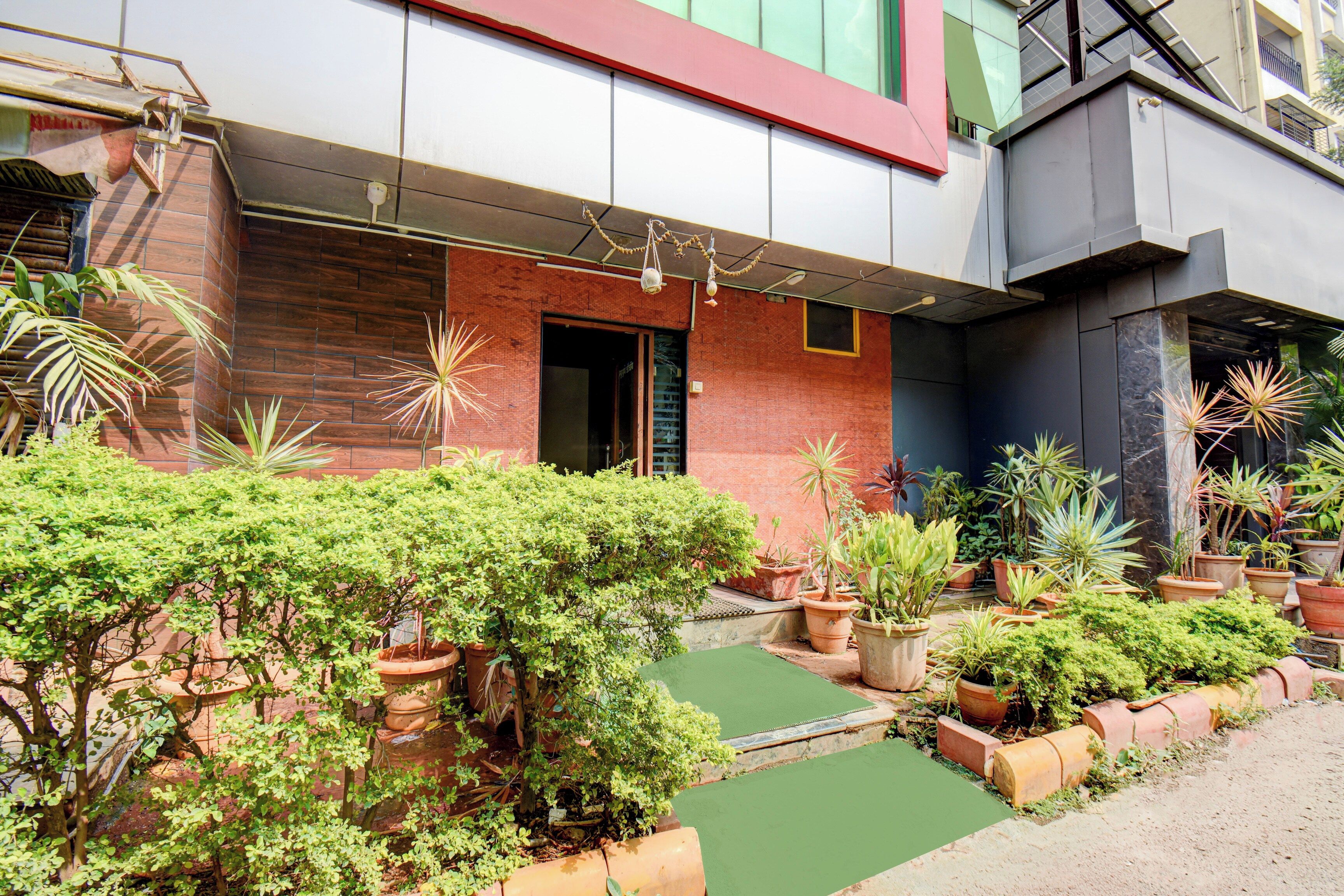 Pátio com plantas em vasos, muro de tijolos e entrada de edifício.