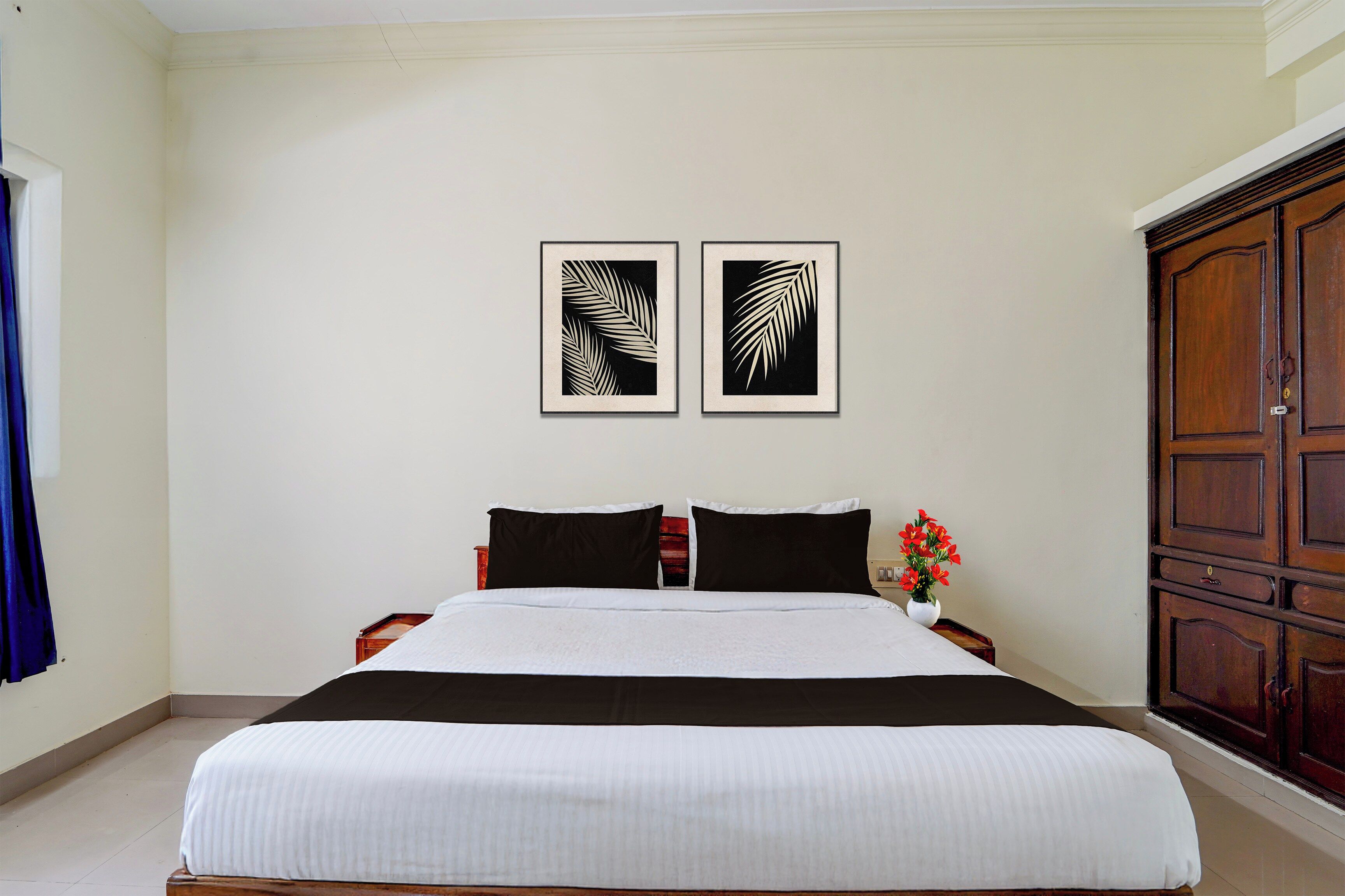 Quarto de hotel com uma cama, duas obras de arte emolduradas, uma mesa de cabeceira, um vaso com flores e um guarda-roupa de madeira.