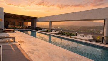 Área de piscina no terraço com vista para a paisagem urbana ao pôr do sol.