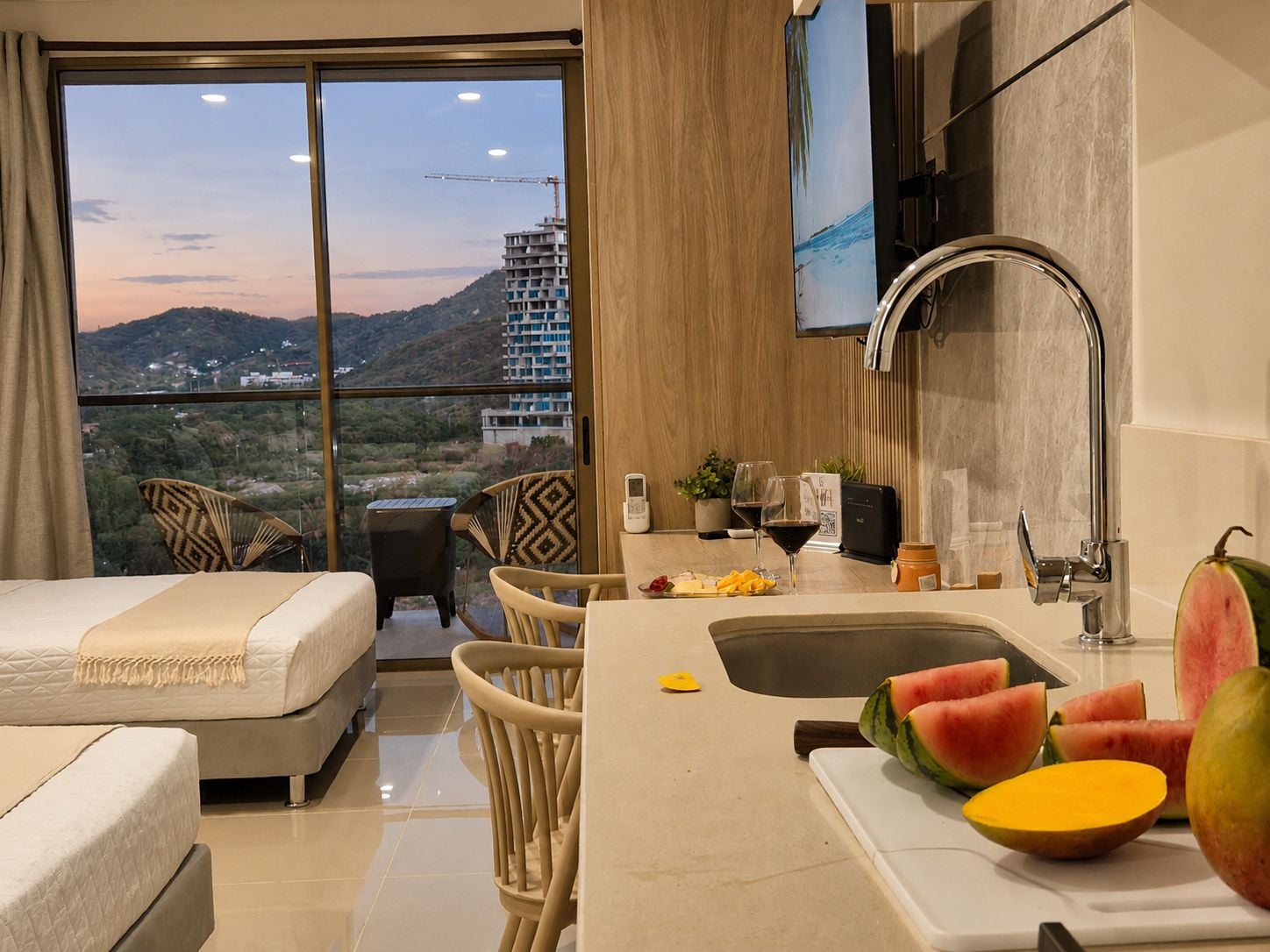 Quarto de hotel com varanda, área de refeições com pia e vista para uma obra.