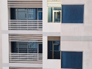 Um edifício de vários andares com persianas horizontais, porta com painel de vidro e parede com destaque em azul.