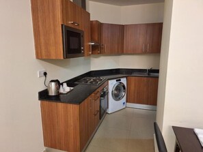 Cozinha compacta com armários de madeira, micro-ondas, fogão e máquina de lavar.