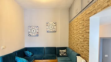 Sala de estar com sofá de canto, dois painéis decorativos fixados na parede, parede com detalhes em tijolo e um radiador.