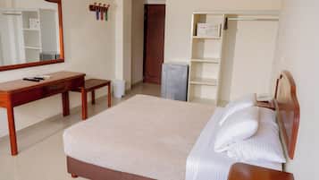 Quarto de hotel com cama, escrivaninha, cadeira, guarda-roupa e espelho.