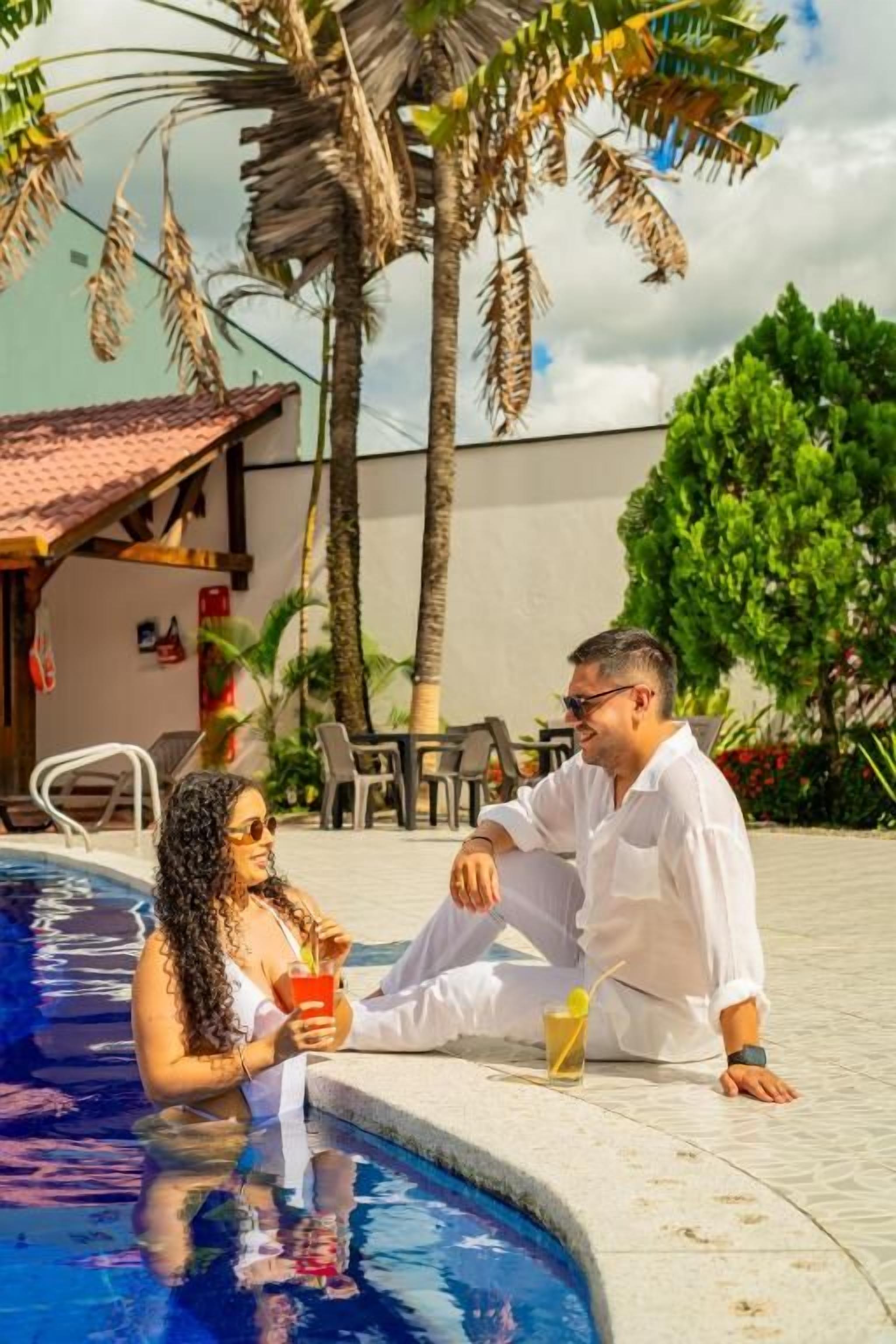 Um casal perto de uma piscina, com uma palmeira e um edifício ao fundo.