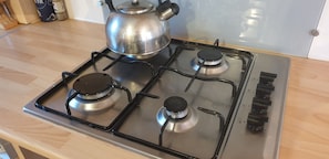 Cozinha com fogão a gás de quatro bocas, chaleira e panela de aço inoxidável.