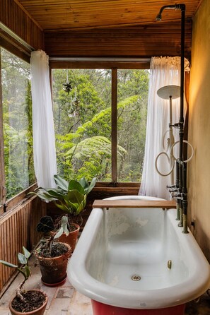 Um banheiro com uma janela grande, banheira e plantas em vasos.