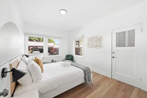 Quarto com cama, cadeira, porta e janela.