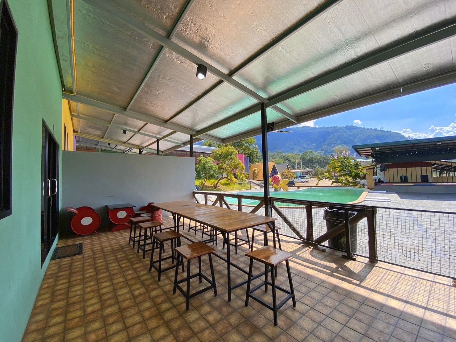 Uma área externa com mesas e cadeiras, um teto coberto e vista para uma piscina e montanhas.