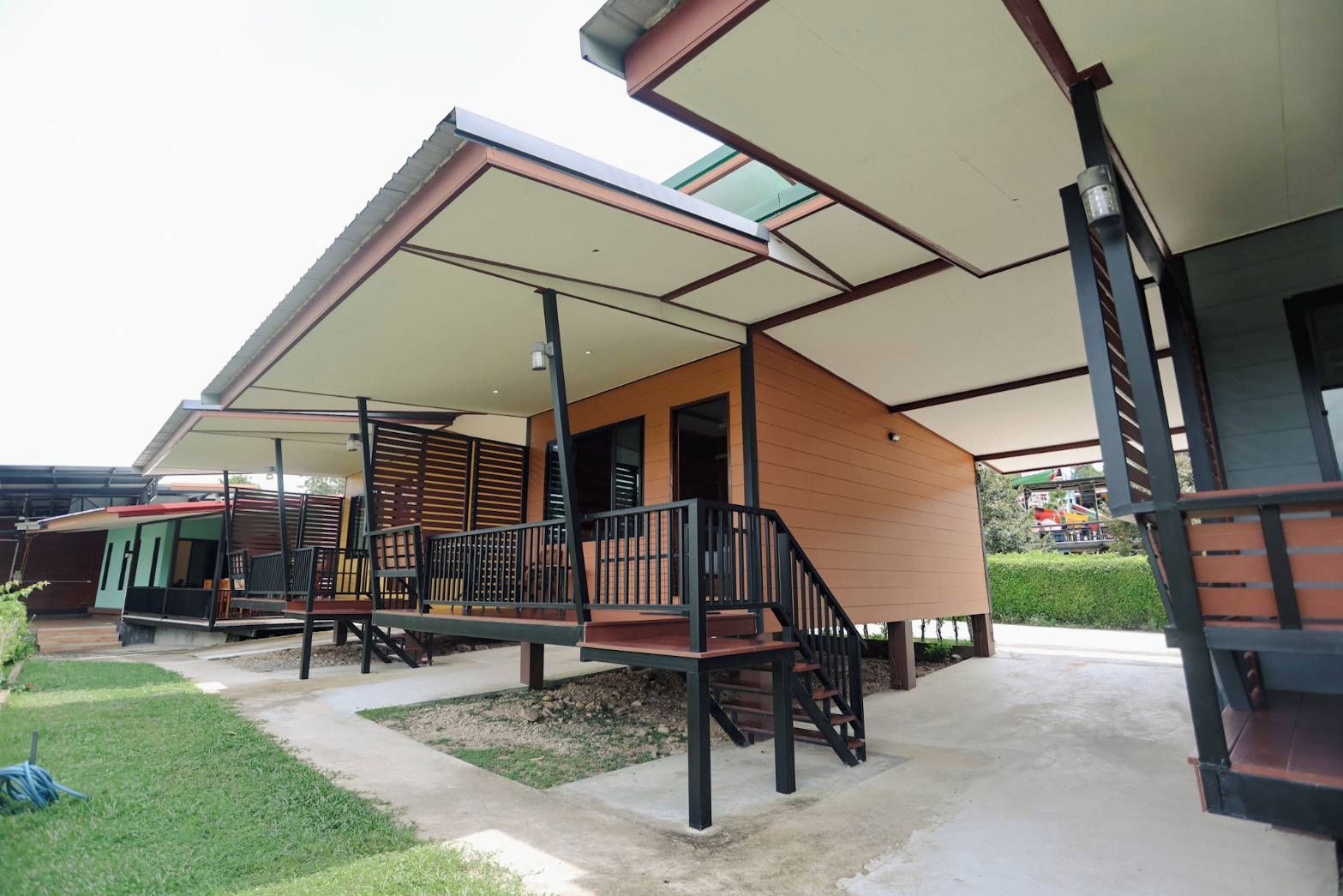 Edifício moderno com área externa coberta, escada e pequeno jardim.