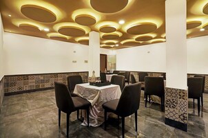 Área de jantar com teto alto, iluminação circular embutida, mesa central com cadeiras e azulejos com padrão.