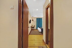 Corredor estreito que dá acesso a um quarto com cama, escrivaninha e cadeira.